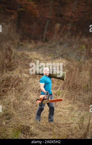 Strong muscular lumberjack with chainsaw, carrying a huge log on his ...