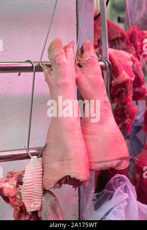 Two pigs hanging in a meat processing facility, one slaughtered and cut ...