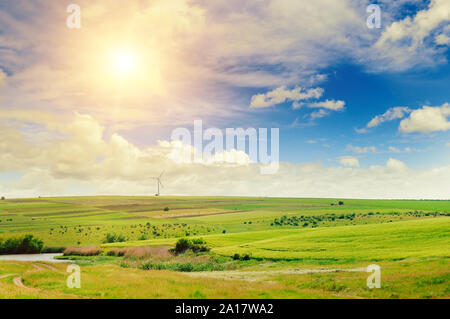 Hilly green field, windmill and sun on blue sky background ...