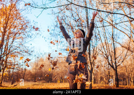 Middle-aged woman throwing leaves in autumn forest. Senior woman having ...