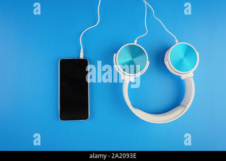 blue white color headphone placed next to handphone on a blue ...