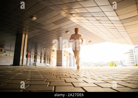 Attractive fit man running fast along countryside road at sunset light ...