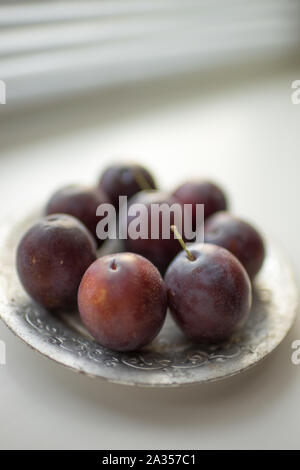 Fresh plums in a plate on a table. Front view Stock Photo - Alamy