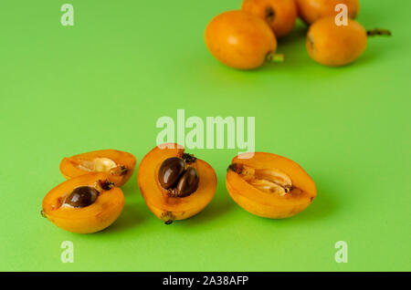 Halves of a Loquat fruits on a bright green background with a space for ...