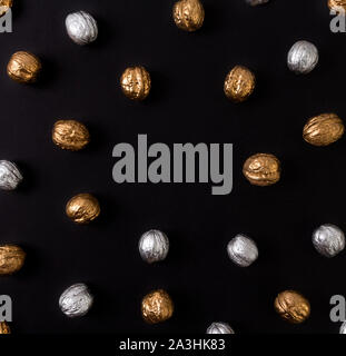 Painted golden and silver walnuts on wooden plate on black background ...