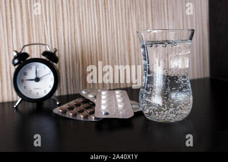 Alarm clock with pill bottles and glass of water on table in room Stock ...