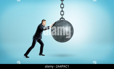 A businessman pushing at a hanging unmoving wrecking ball. Heavy burden ...