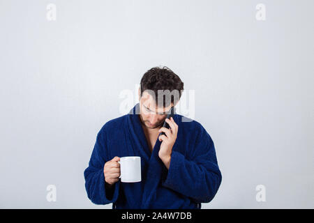 Young man wearing a bathrobe drinking a cup of coffee in the morning ...