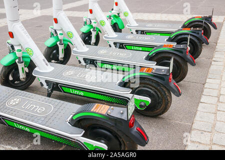A line of electric scooters from Lime, Dott and Tier for hire / rental parked on a pavement in ...