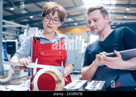 Workers measuring a metal workpiece Stock Photo - Alamy