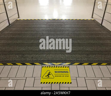 Beware uneven floor warning sign on yellow board in front of escalator ...
