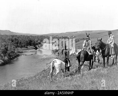 Three Piegan Indians and four horses on hill above river, Edward S ...