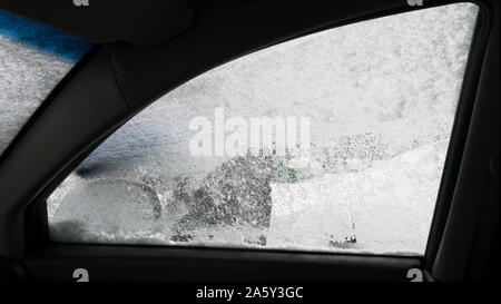 Closeup of frozen car window - view from inside the car. Man clears car ...
