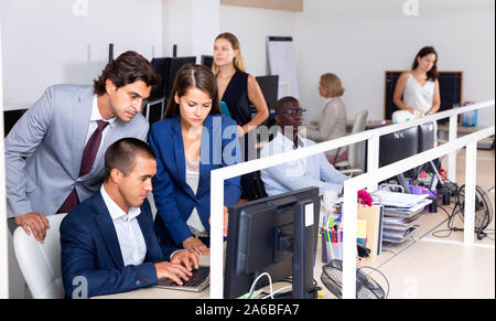 Focused young business people grouped around computer monitor ...