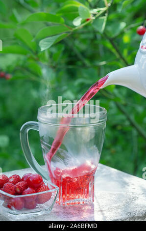 Cup of hot berry tea is poured from a teapot into a glass Cup, cookies ...