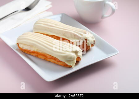 Eclairs with White Chocolate Glaze in a dish on pink background. One of ...