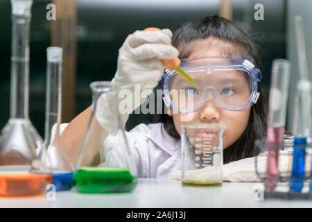 Cute little girl wearing safty goggle and lab coat making experiment in ...