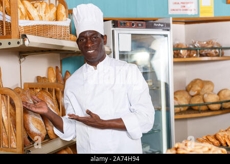 Successful baker wearing white uniform working behind counter in ...