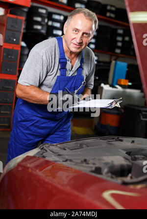 Professional auto mechanic recording list of works on car repair in ...