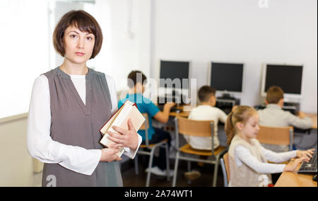 Strict female teacher standing foreground in classroom Stock Photo - Alamy