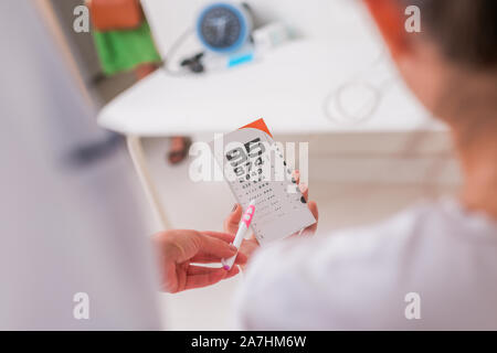 Woman ( girl )reviewing eyesight closing eye with hand. Eye test. Eyesight vision exam chart ...