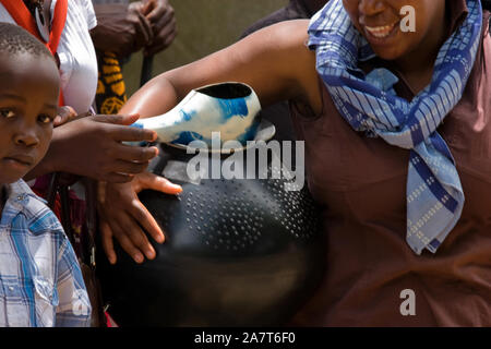 The hands of a woman carrying a black Zulu beer pot containing marula ...