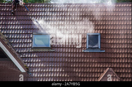 Man cleaning the roof of a house using a high pressure water jetwash ...