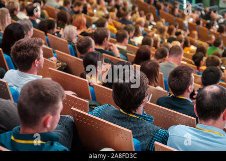 Business conference attendees sit and listen to lecturer, rear top view ...
