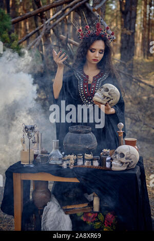 Attractive, wicked, long-haired witch in a black, long dress with cape ...