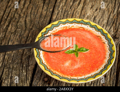 Smooth red gazpacho in rustic gray bowl with basil leaves on top. Fresh ...