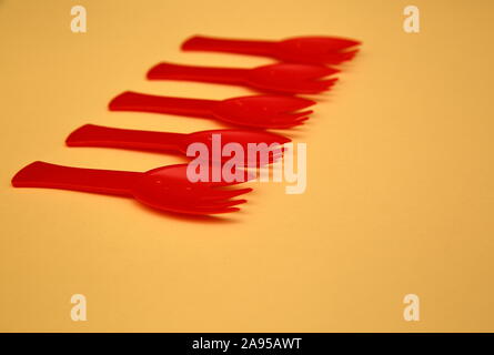 Five red plastic forks lie next to each other isolated on pastel peach ...