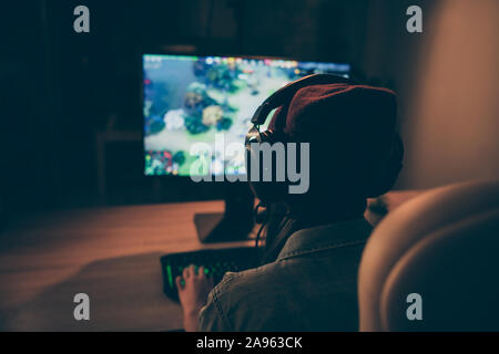 Rear view of female gamer girl with headset sits in a dark room behind ...