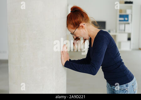 Frustrated businesswoman banging head against the desktop in front of a ...