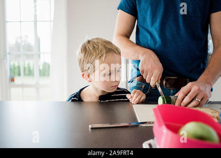 father making his kids packed lunches for school whilst daughter looks ...