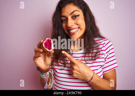 Young beautiful woman holding amethyst gemstone over isolated pink ...