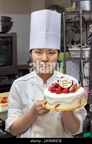 A Japanese female pastry chef showing a cake decorated with cream and ...