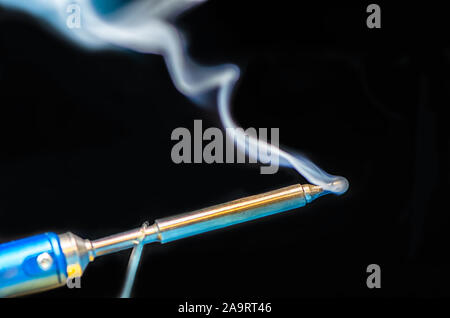 soldering iron with smoke on a black background. Electrical ...