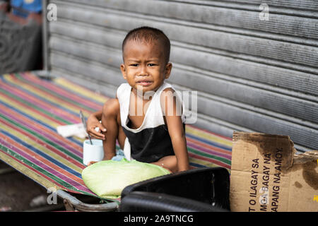 A young Filipino boy sitting on a sidewalk,seemingly has just been ...