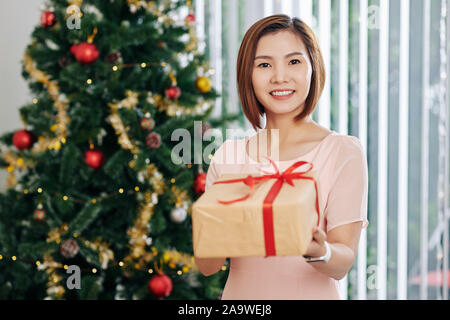 Pretty young woman with Christmas gift box sitting on sofa at home ...