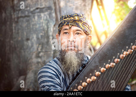 Asian old man playing kecapi with tree background. Kecapi is a ...