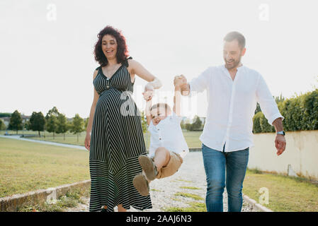 Parents swinging their smiling son in an urban park on an autumn day ...