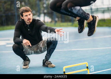 Hurdle jumping training outdoors. Sporty woman jumping over the hurdle ...
