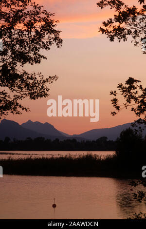 Scenic view of Forggensee lake and silhouette mountains during sunset ...