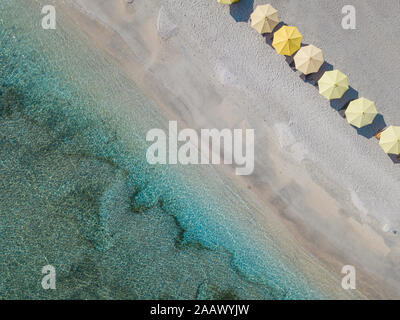 An aerial shot of a yellow beach umbrella and a person in a swimsuit ...