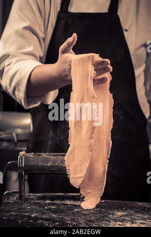 The chef makes fresh pasta from scratch. Wooden table. Photo in brown ...