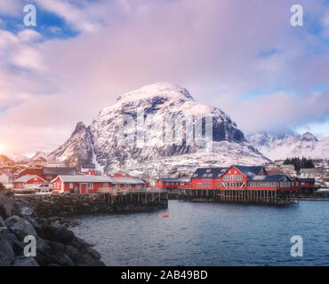 Red traditional rorbuer in small village at sunset in winter in Lofoten ...