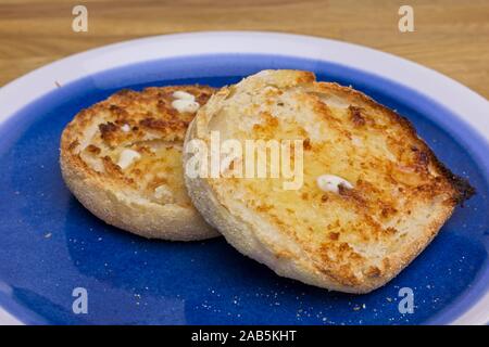 Hot toasted muffins cut in half and buttered on a blue plate Stock ...
