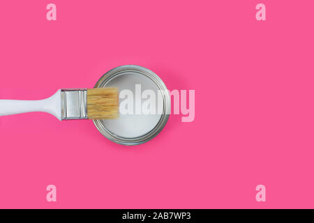 Brush with black handle on open can of white paint on blue background ...