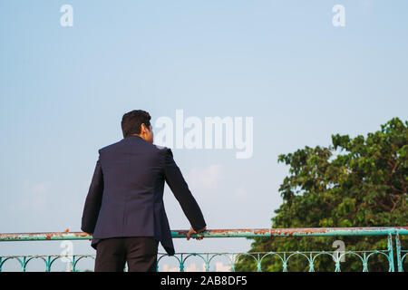 Rear view of Asian businessman standing with raised hand on the rooftop ...