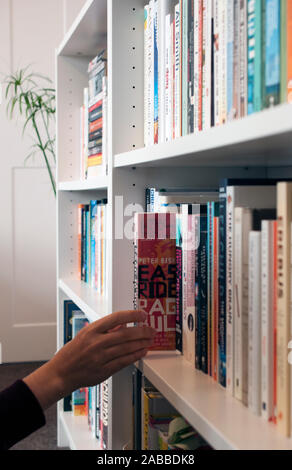 Chosing a book - a person picking out their next read form a shelf full ...